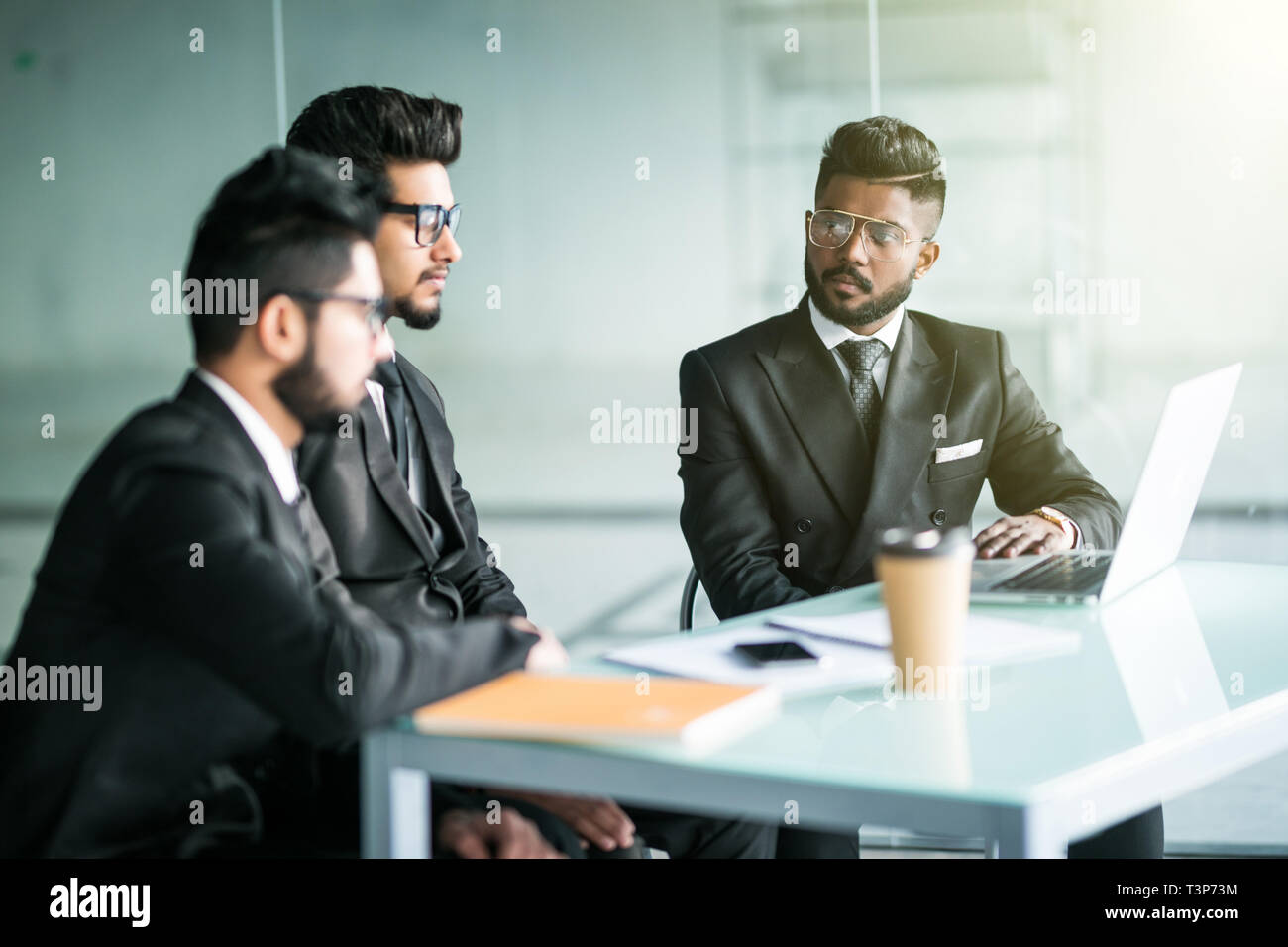 Three Businessmen Sitting Around Table Meeting In Modern Open Plan ...