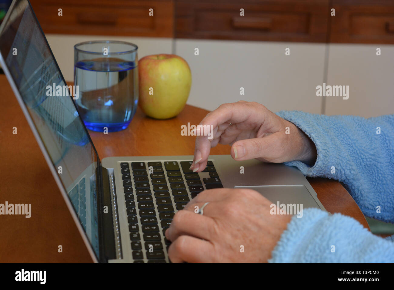 woman working on a laptop computer with an apple and glass of water on ...