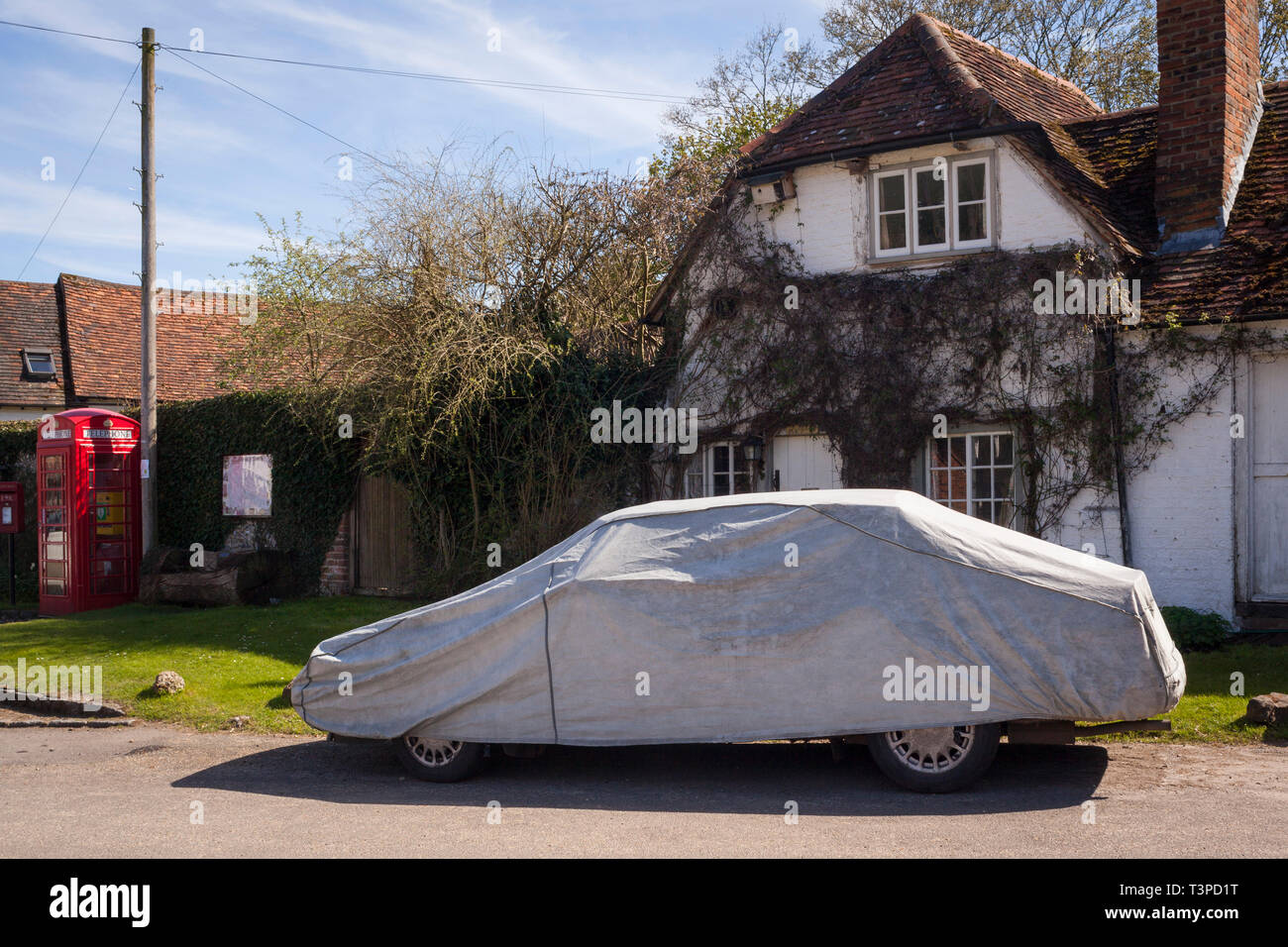 A large classic car with a grey car cover and a red telephone box in ...