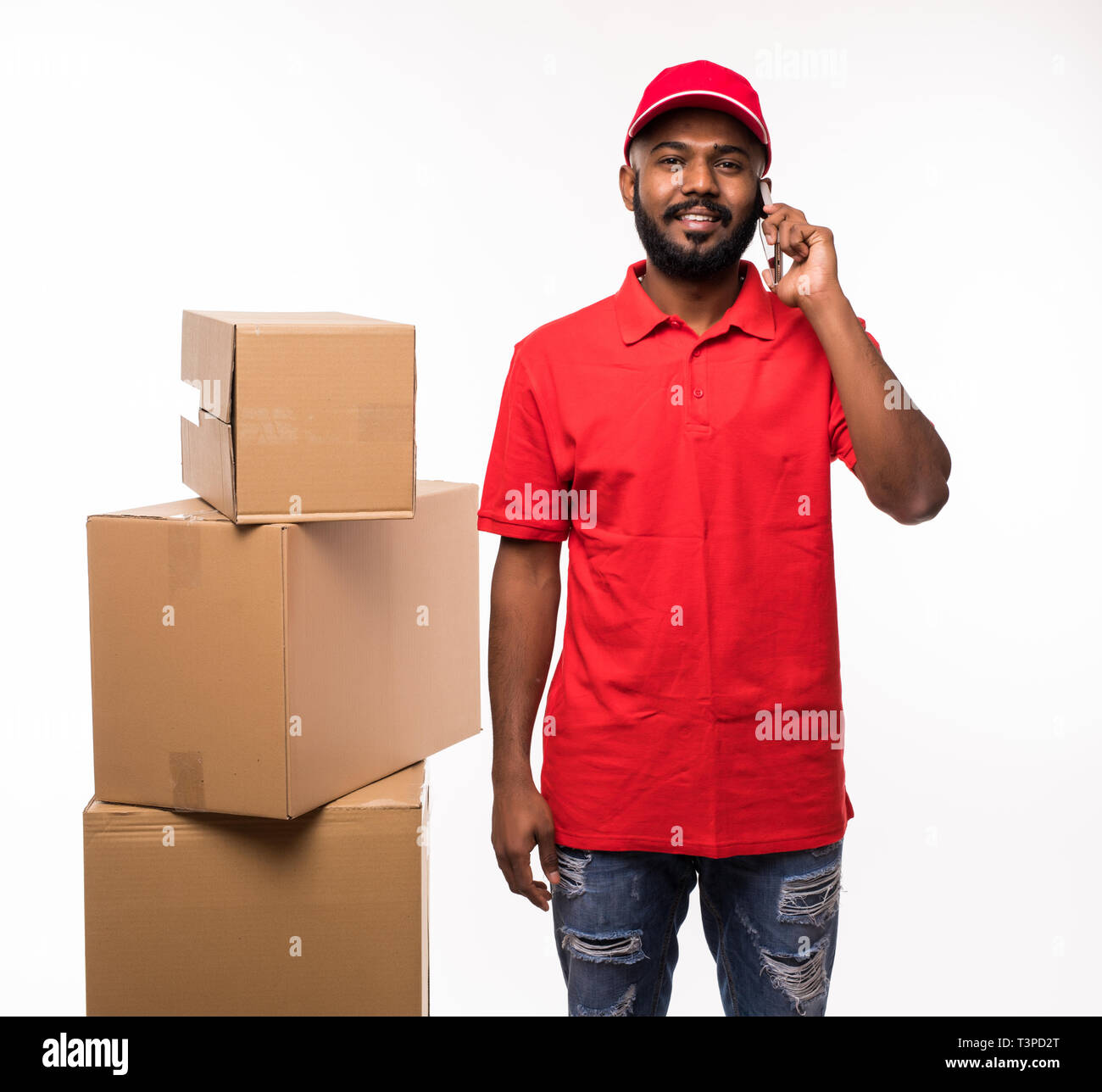 Image of a handsome happy young delivery man talking by mobile phone in ...
