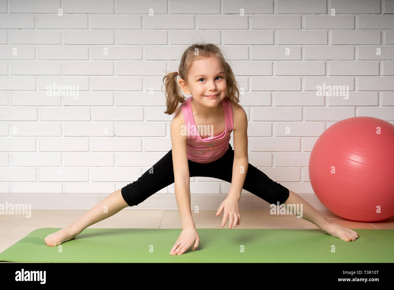 Cheerful little girl doing sports exercises on the mat at home ...