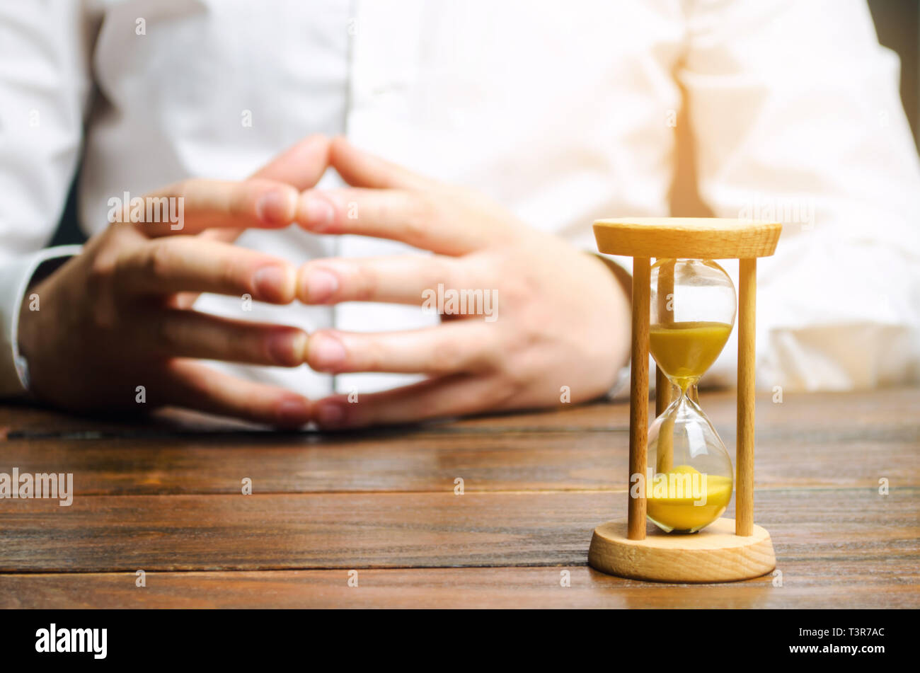 An hourglass and businessman holds his hands in the lock. Job interview ...