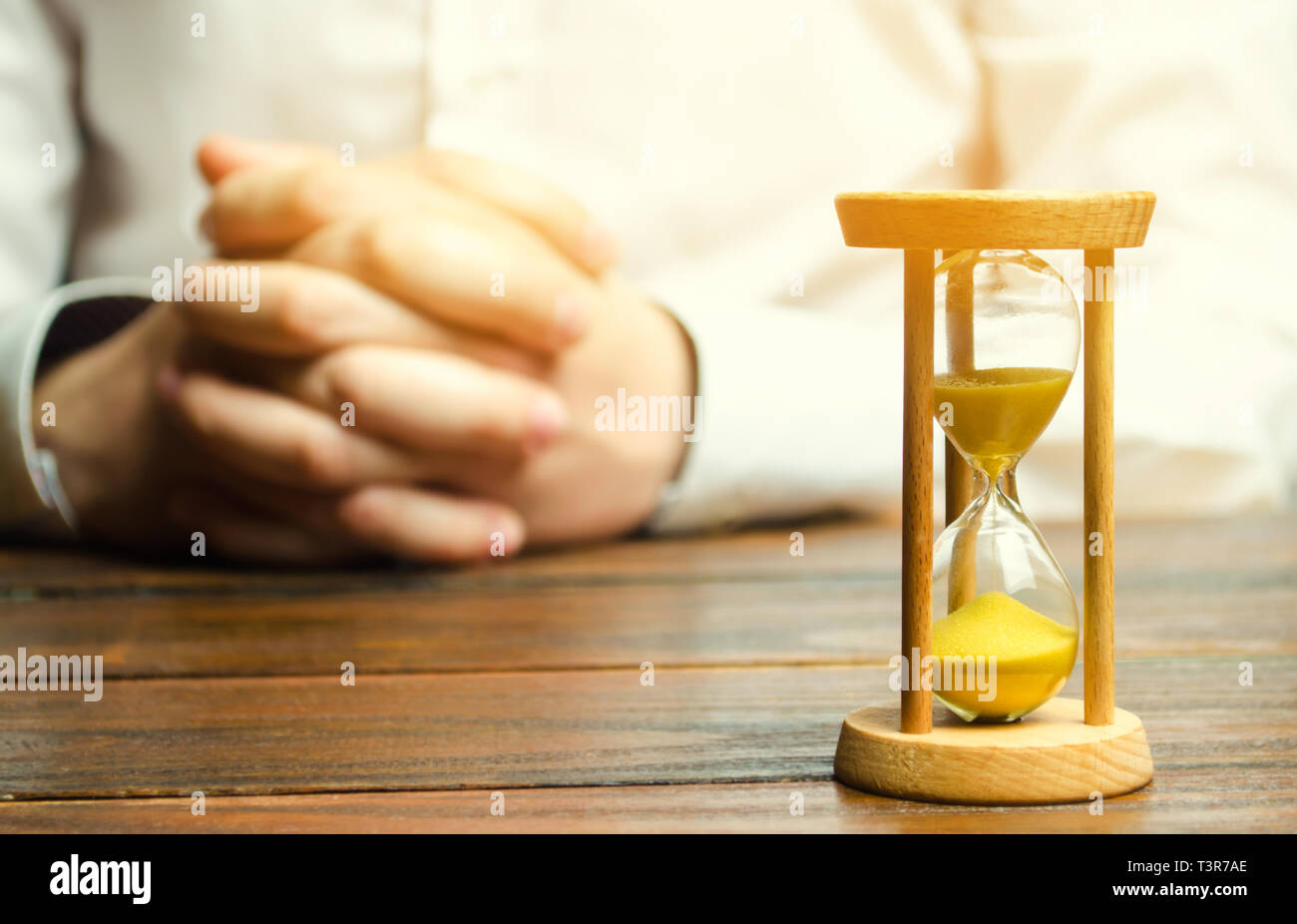 An hourglass and businessman holds his hands in the lock. Job interview ...