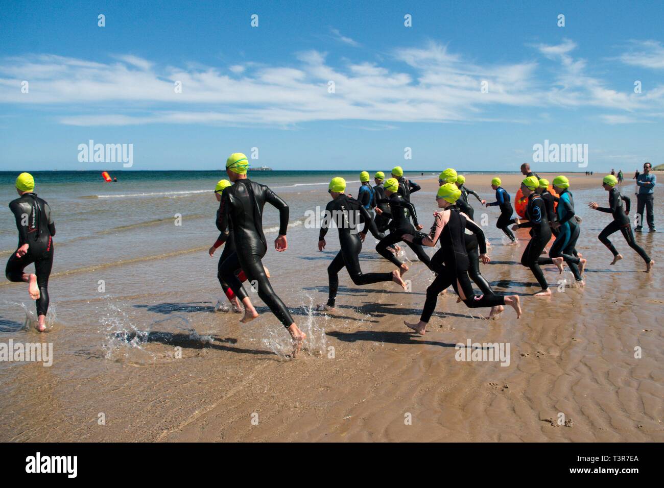 Triathletes running into the sea on the beach at Bamburgh at the start ...