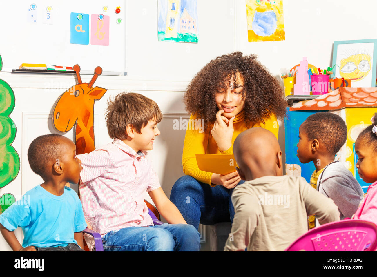 Teacher in kindergarten reading a book to kids Stock Photo - Alamy
