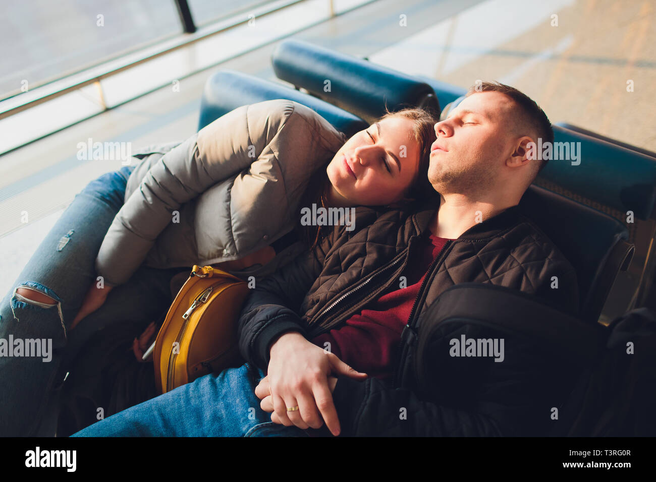 Young couple sleeping on the chairs at the waiting room of the airport. Long waiting for the ...