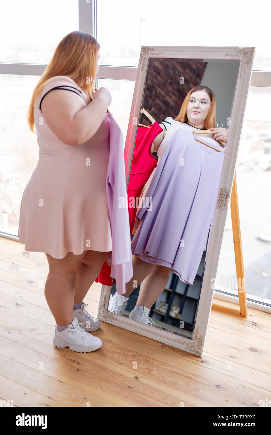 Pleasant good looking woman choosing between dresses Stock Photo - Alamy
