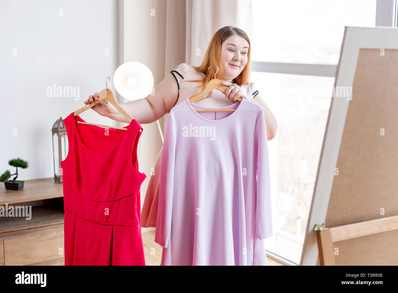 Joyful positive woman comparing two different dresses Stock Photo - Alamy