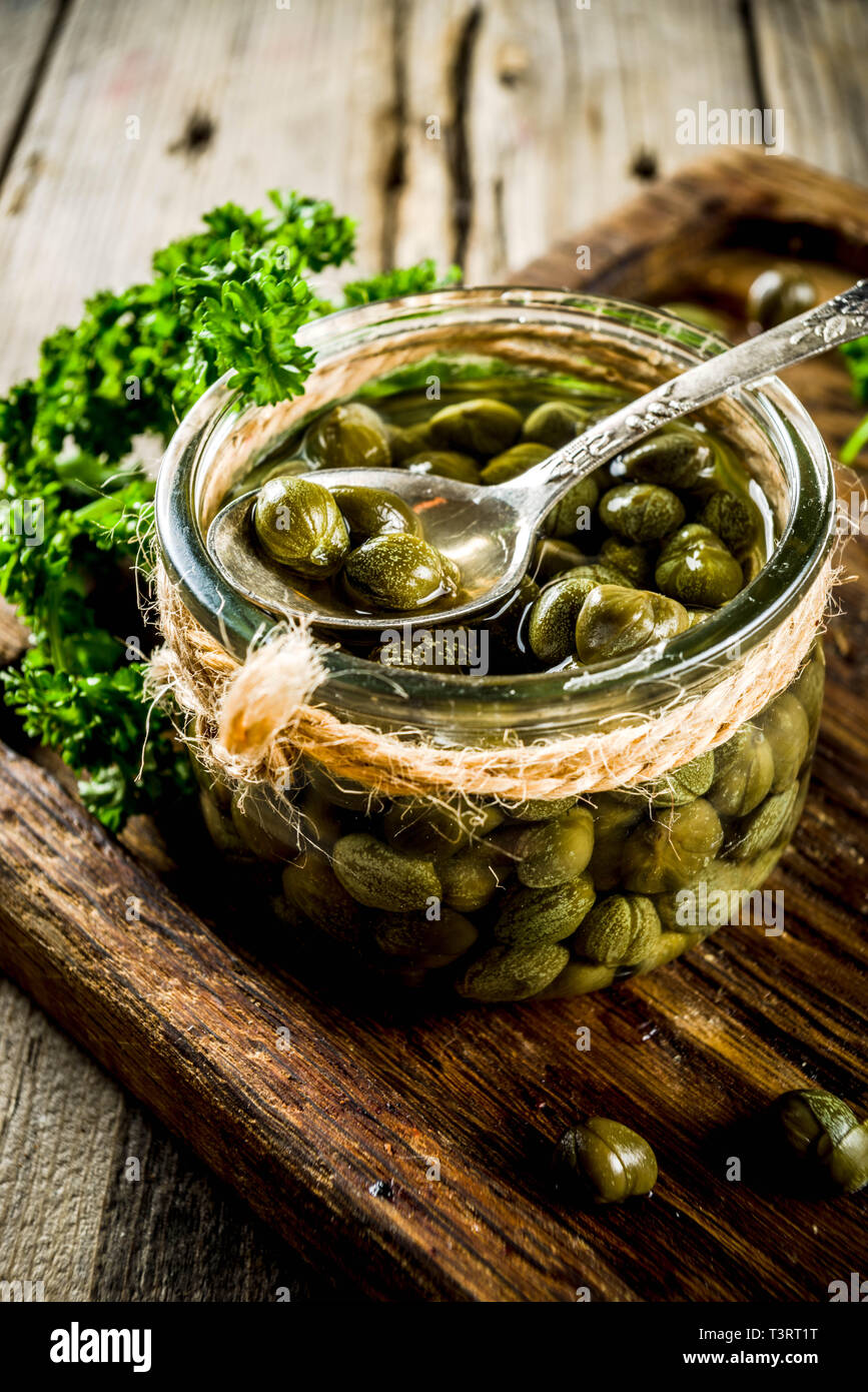 Pickled capers in little jar, with herbs on rustic wooden background ...