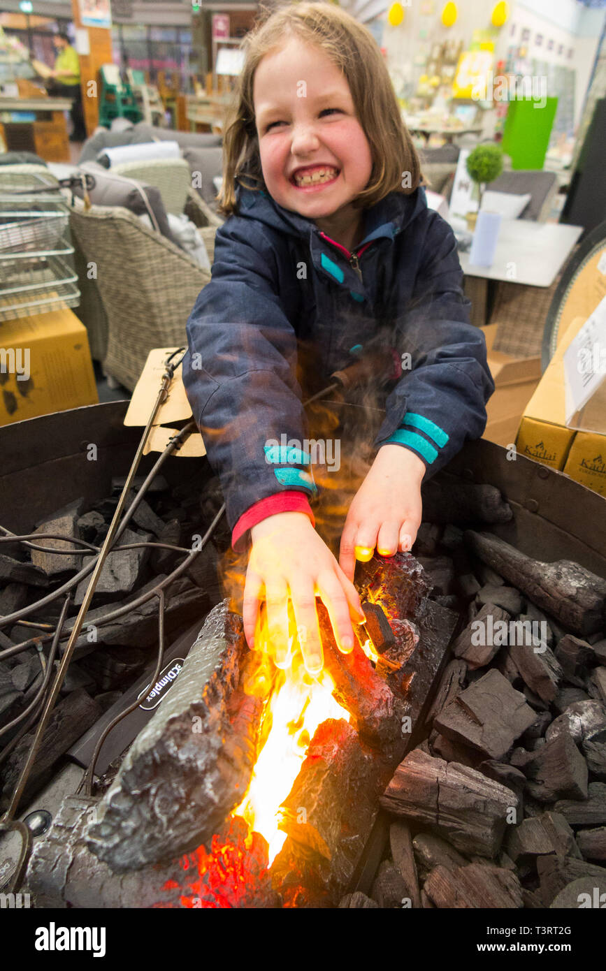 Young girl holds her hand in the fake flame effect fire of a barbecue ...