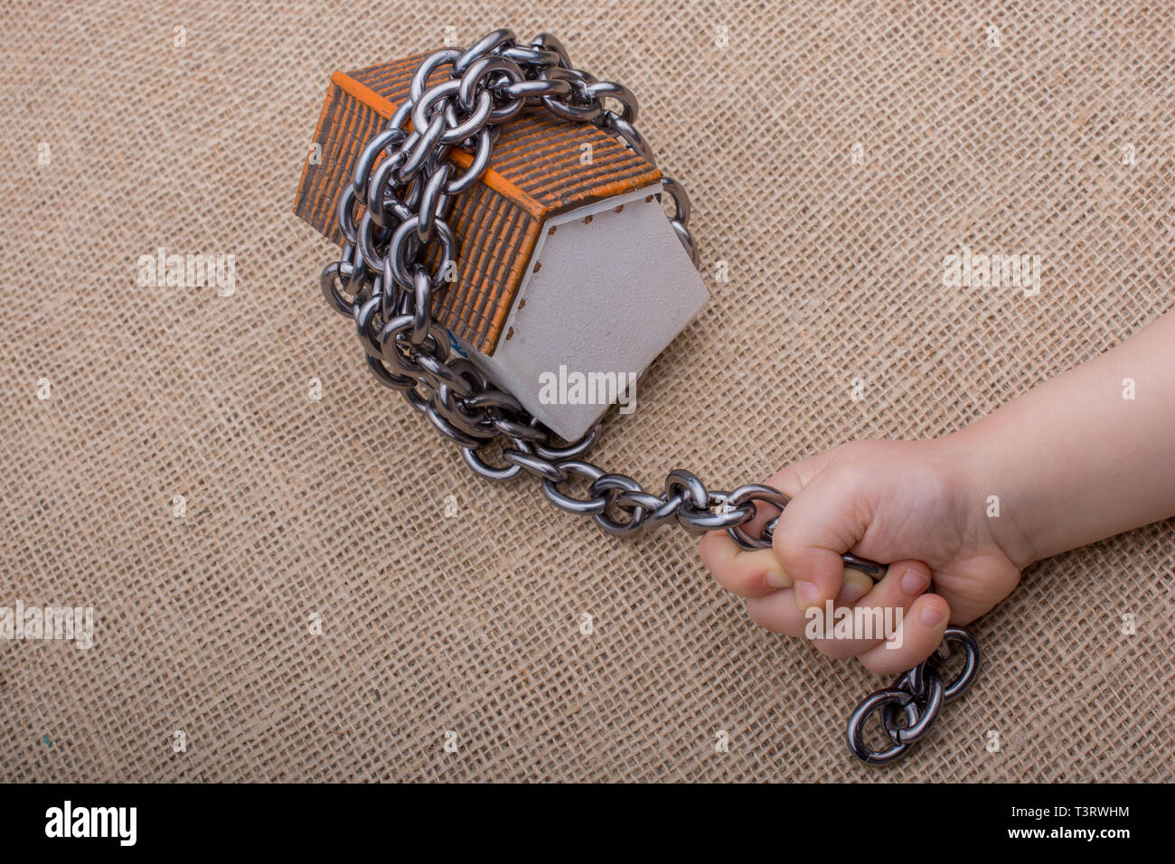 Little hand holding a chain around a model house on a brown background ...