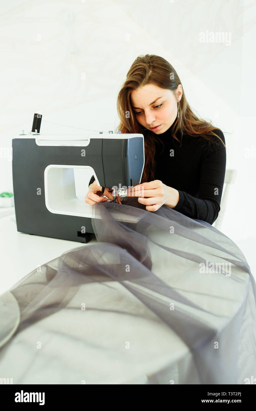 Young dressmaker woman sews clothes on sewing machine. Smiling ...