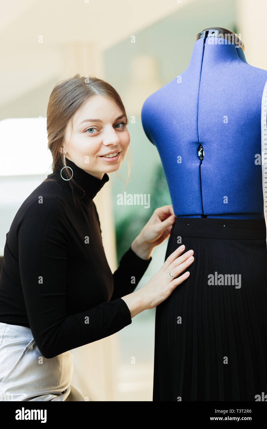 A young seamstress woman sets clothes on the mannequin. Portrait of ...