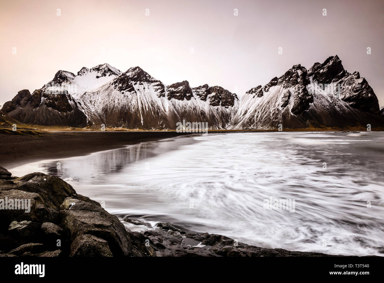 Ocean waves on beach under snowy mountains Stock Photo - Alamy