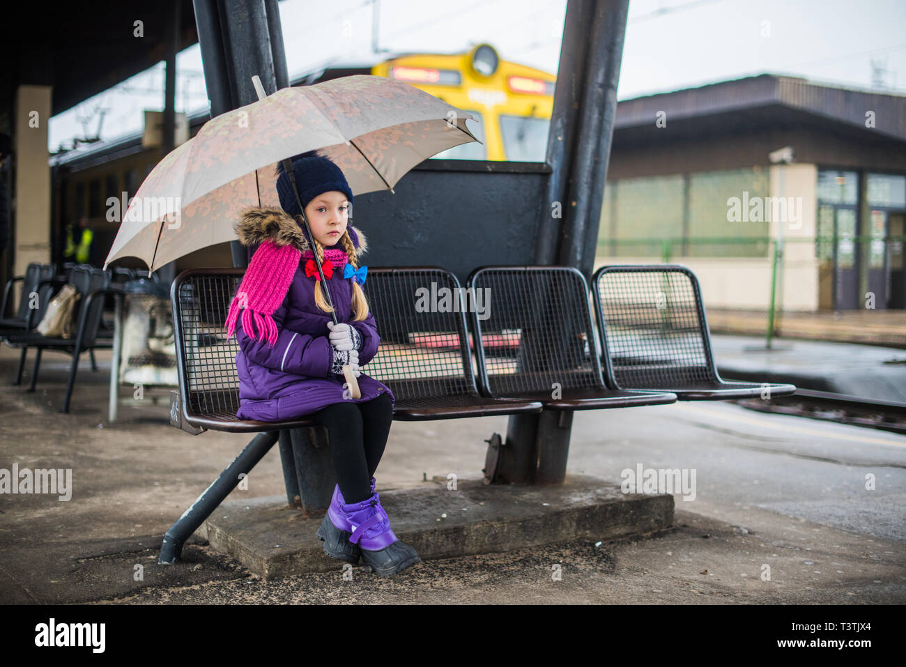 Little child sitting on platform with an umbrella on a railway train ...