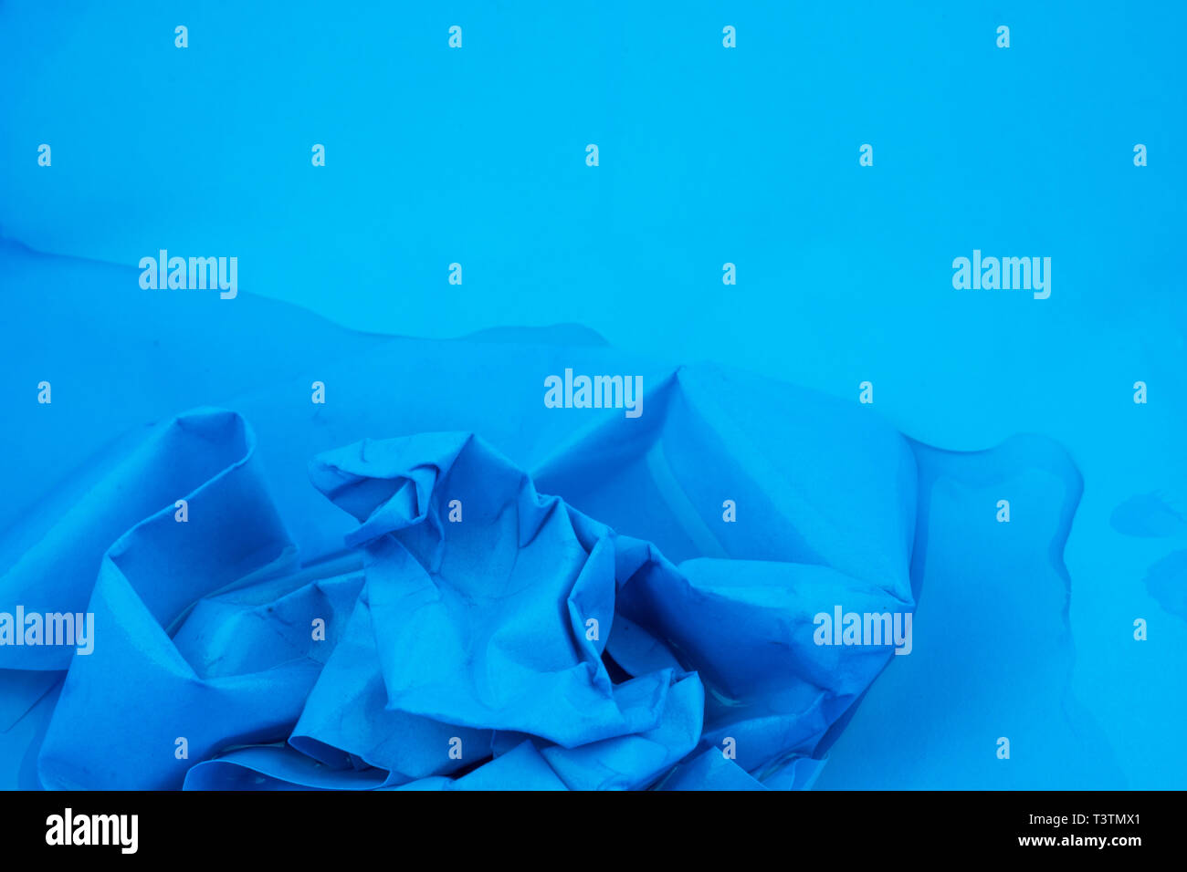 Crumpled paper put in water in blue background Stock Photo - Alamy