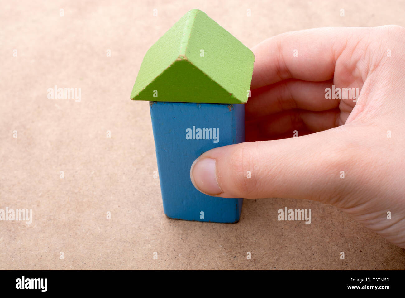 Hand holding a house formed out of building blocks s on a brown ...