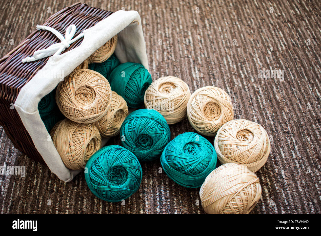 on the floor is an inverted basket with beige and green knitting yarns ...