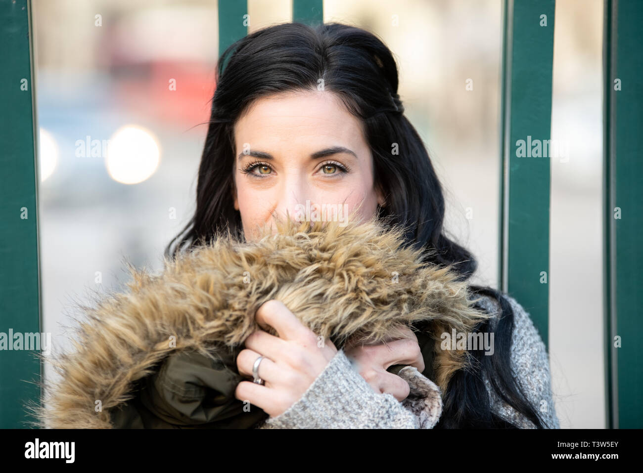 Portrait of brunette woman hugging her own coat to wrap herself up ...