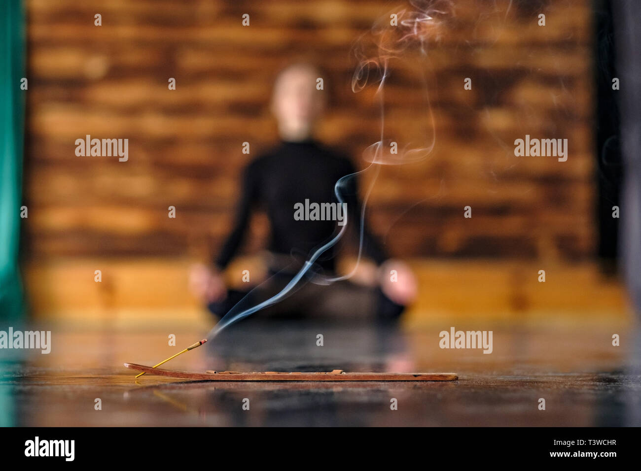 smelling burning stick and blurred woman at the back in lotus yoga pose ...