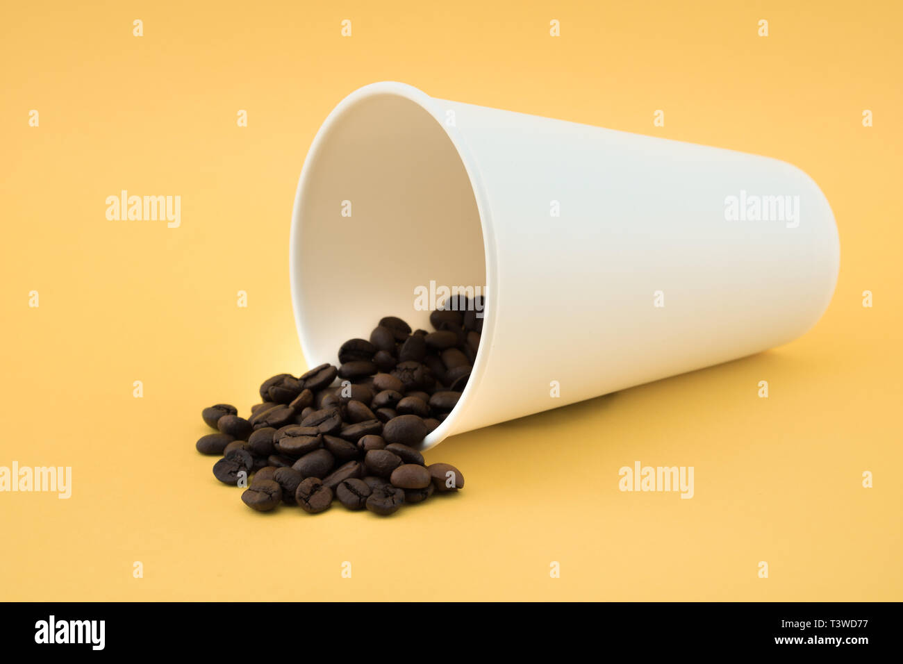 Paper coffee cup with spilled coffee beans, yellow background. Roasted ...
