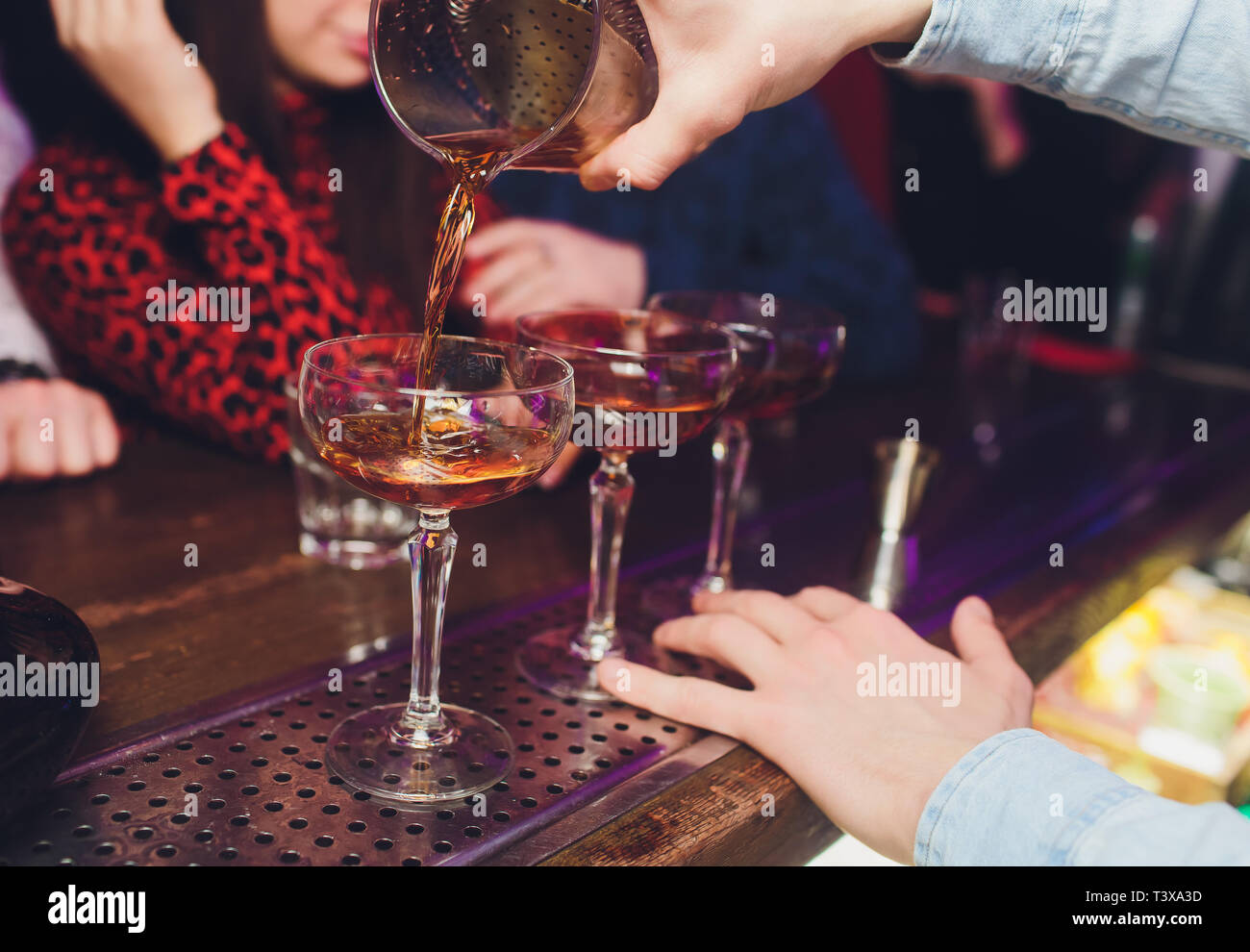 Male bartender is making cocktail pouring alcohol from shaker to glass ...