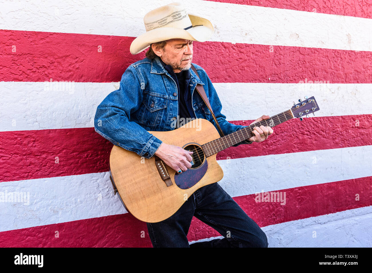 Old cowboy with gray beard stands next to a white and red wall Stock ...