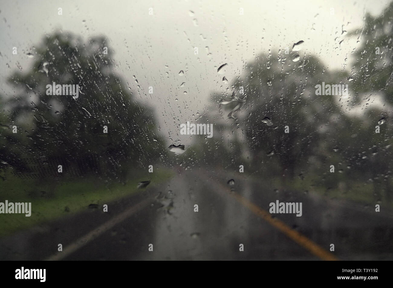 Rain drops on the car glass window with road in rainy season abstract ...