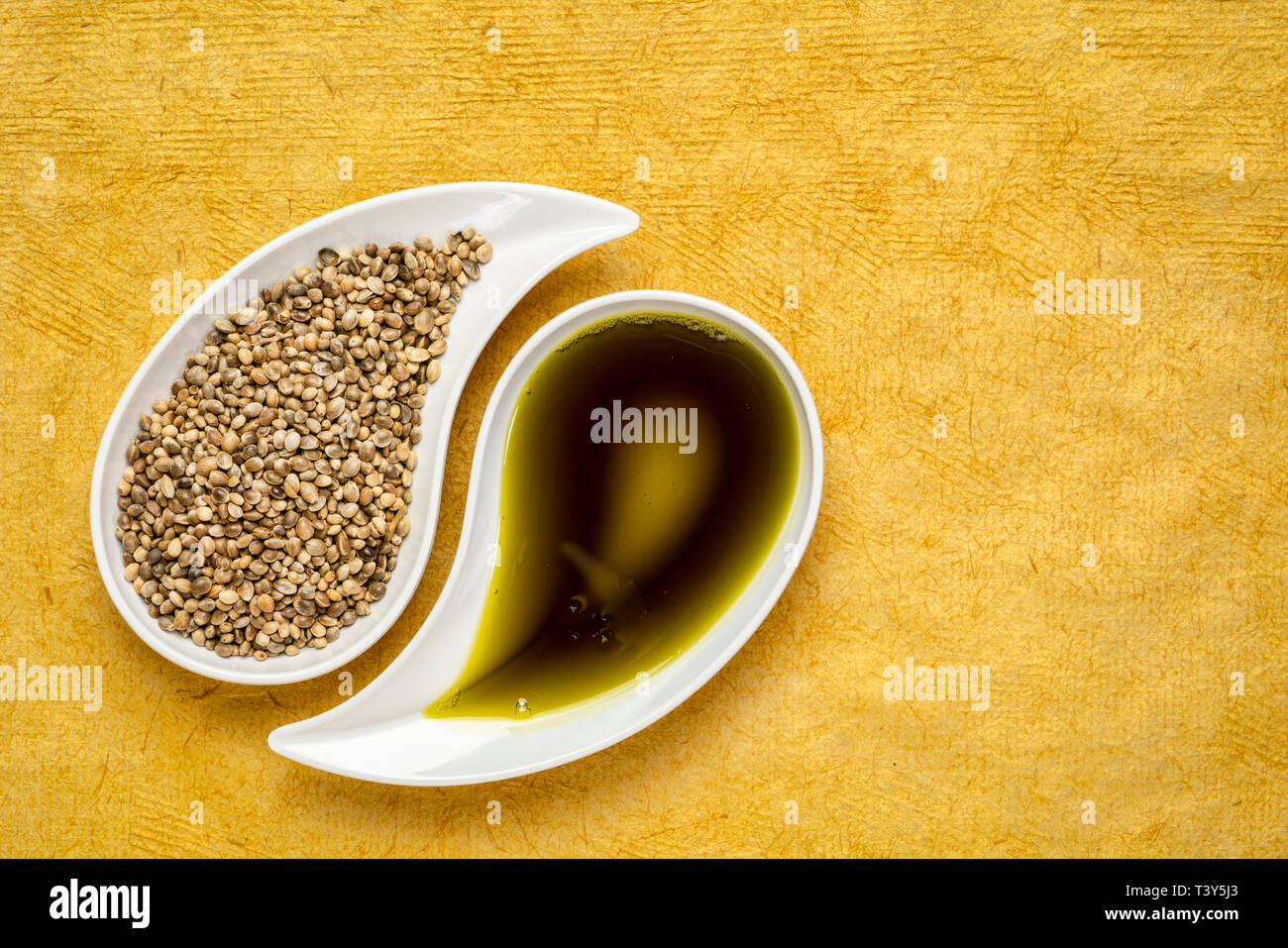dry hemp seeds andoil in small teardrop bowls against yellow textured ...