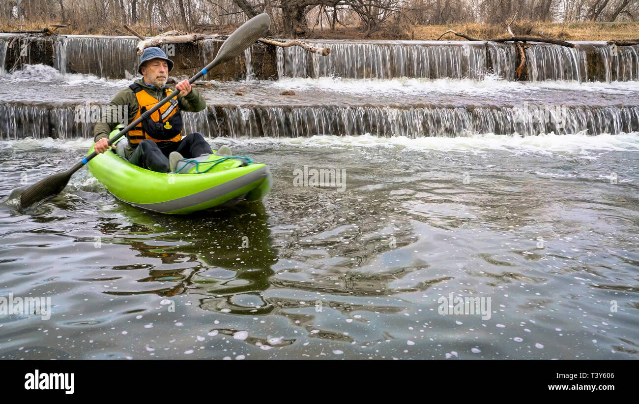 senior kayaker is paddling a whitewater inflatable kayak on a river ...