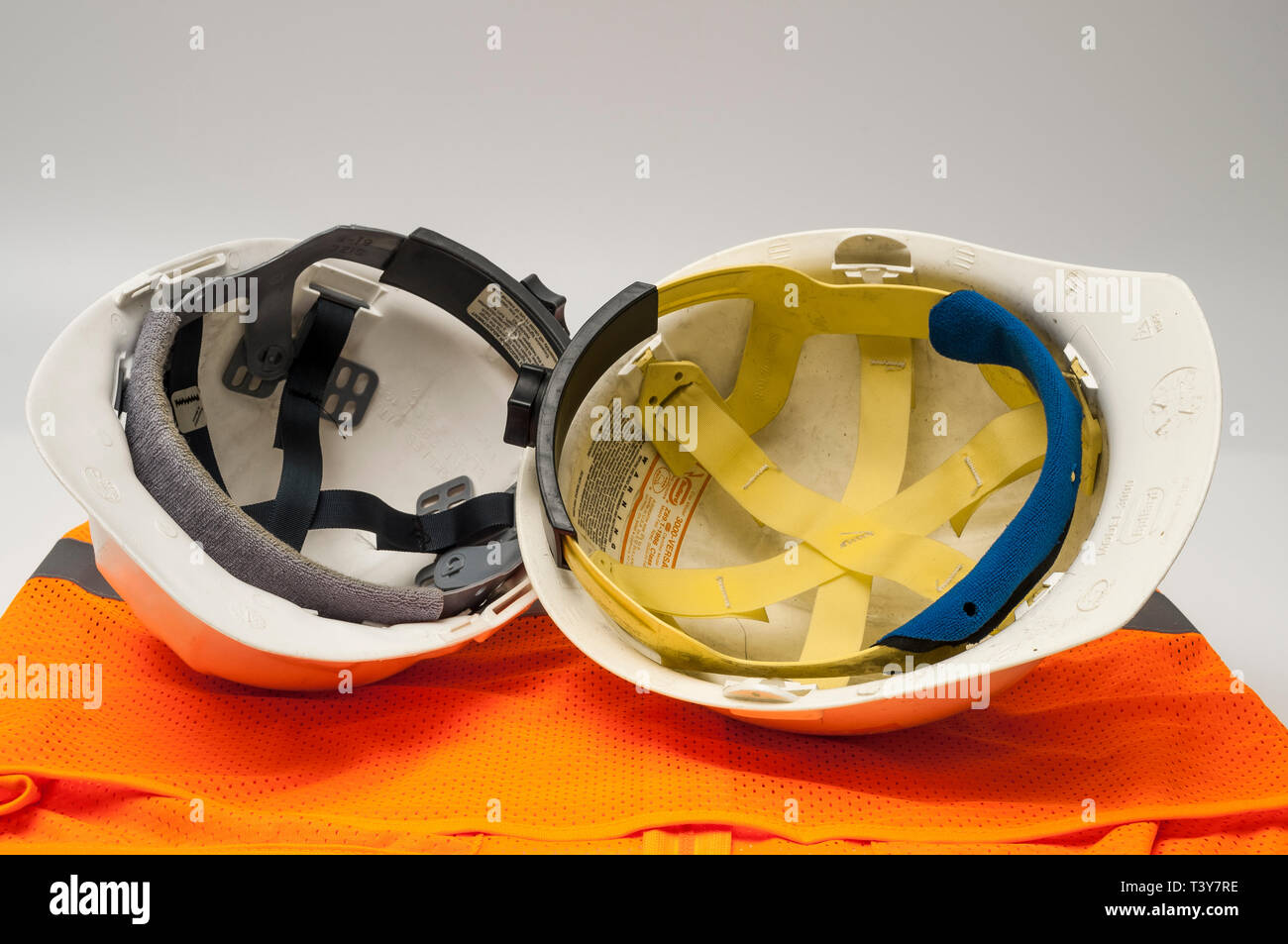 Two old worn hard hats and an orange vest showing inner webbing Stock ...