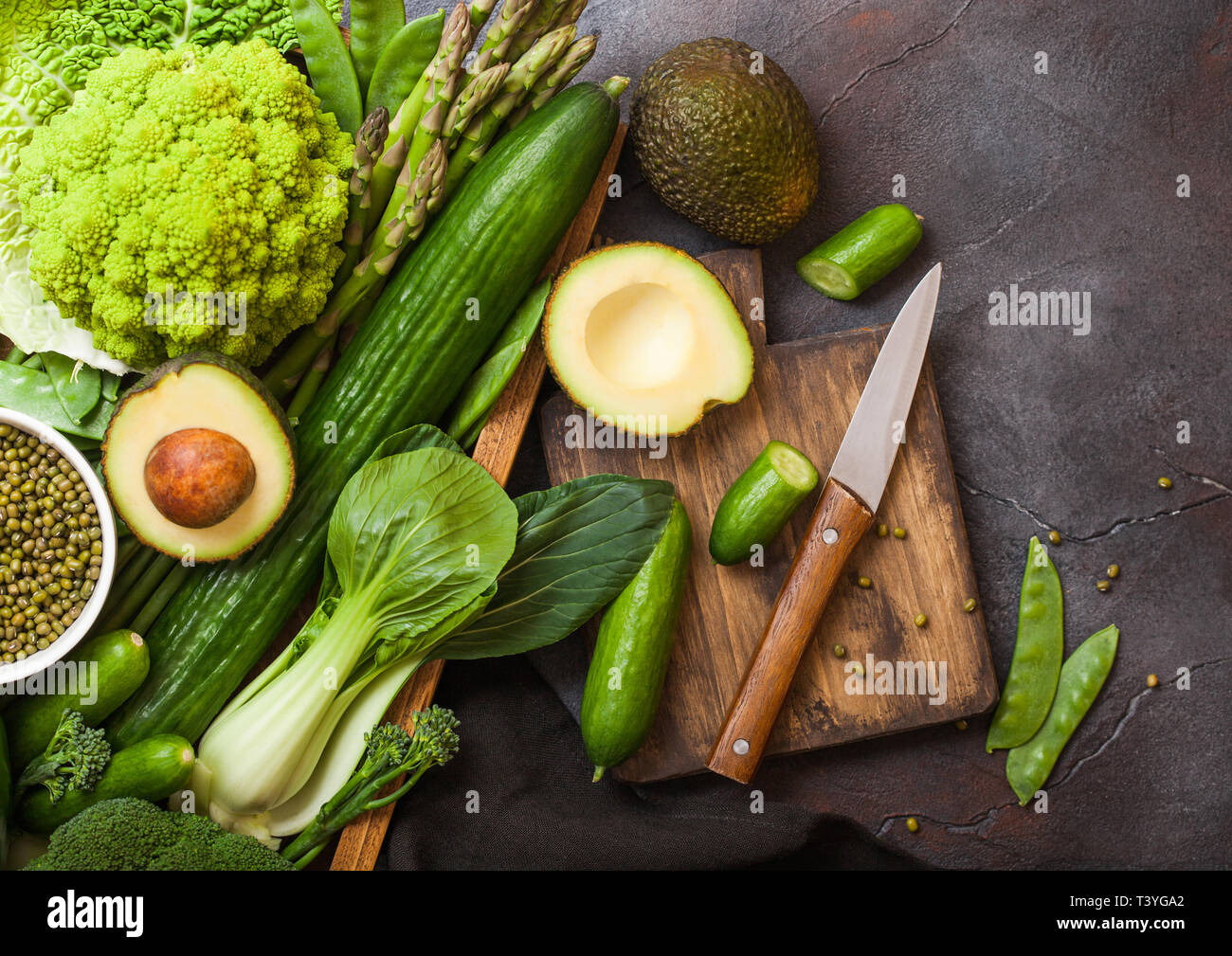 Assorted green toned raw organic vegetables in wooden box on dark stone ...