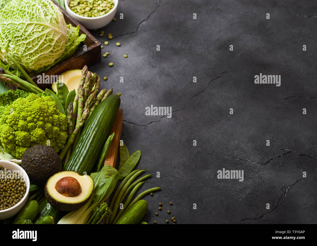 Assorted green toned raw organic vegetables on dark background. Avocado ...