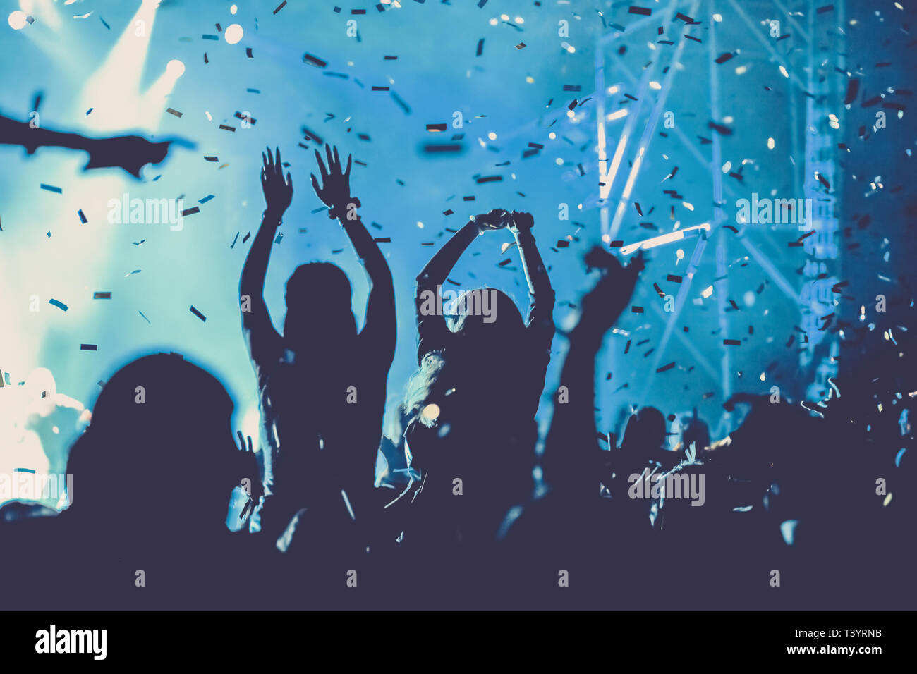 cheering crowd with raised hands and falling confetti at concert ...
