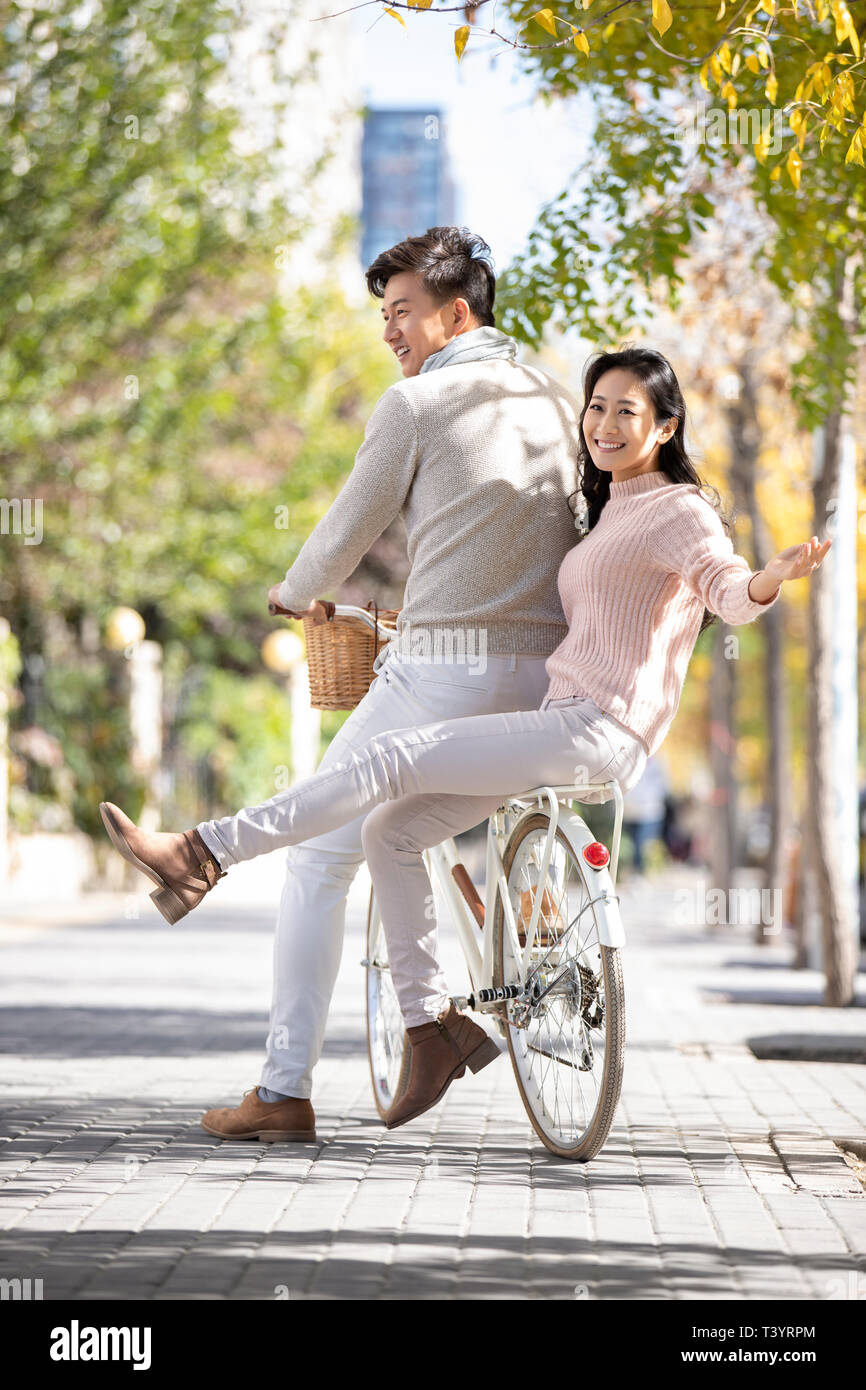 Happy young couple riding bike together on street Stock Photo - Alamy