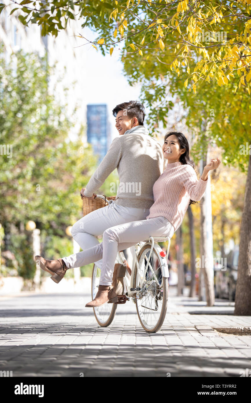 Happy young couple riding bike together on street Stock Photo - Alamy