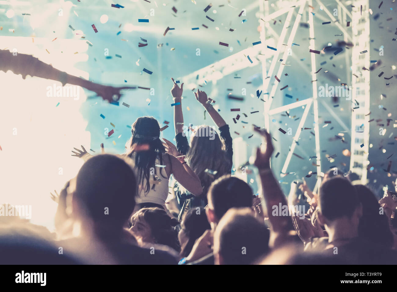 cheering crowd with raised hands and falling confetti at concert ...