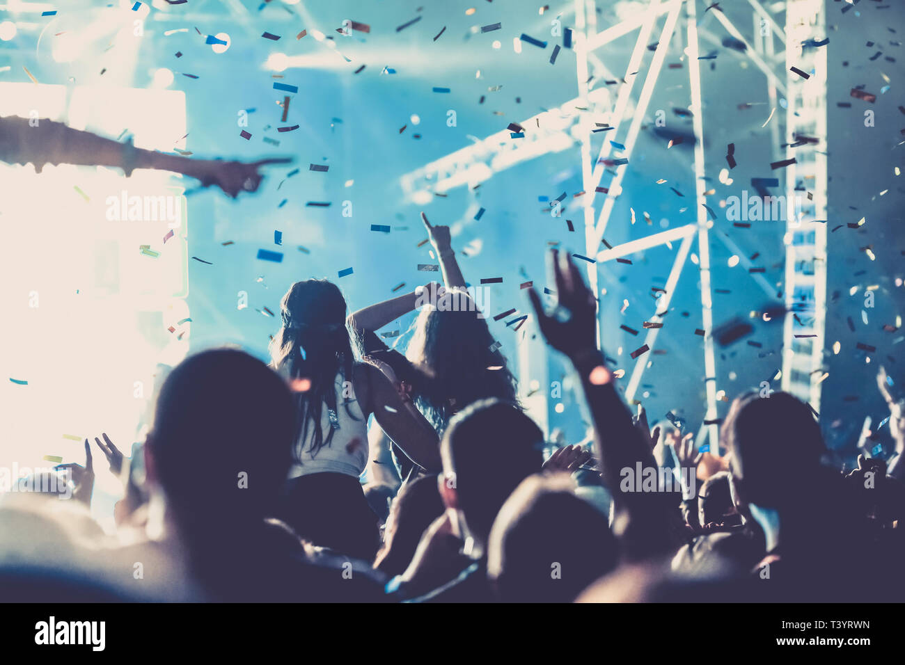 cheering crowd with raised hands and falling confetti at concert ...