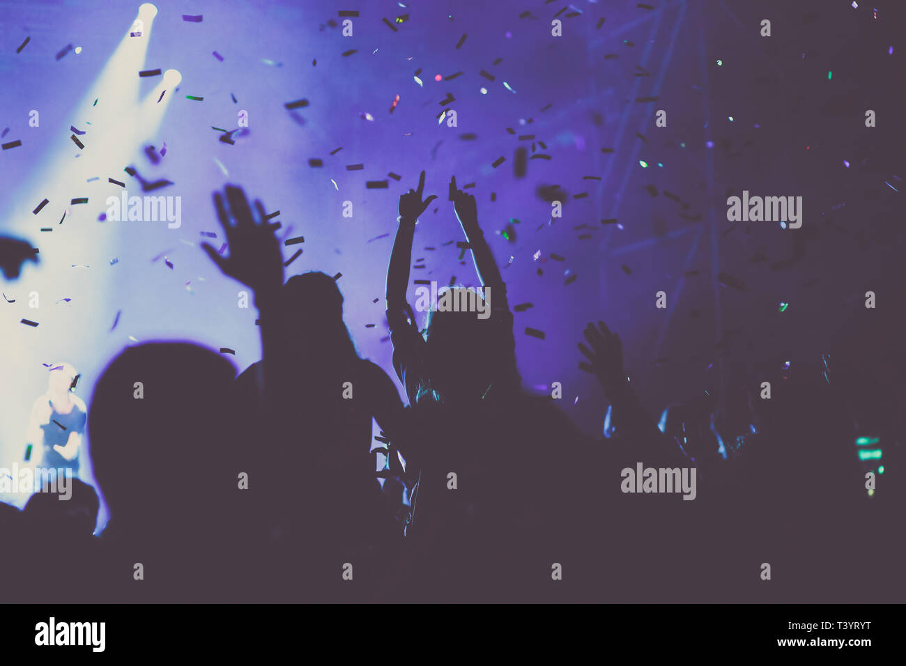 cheering crowd with raised hands and falling confetti at concert ...