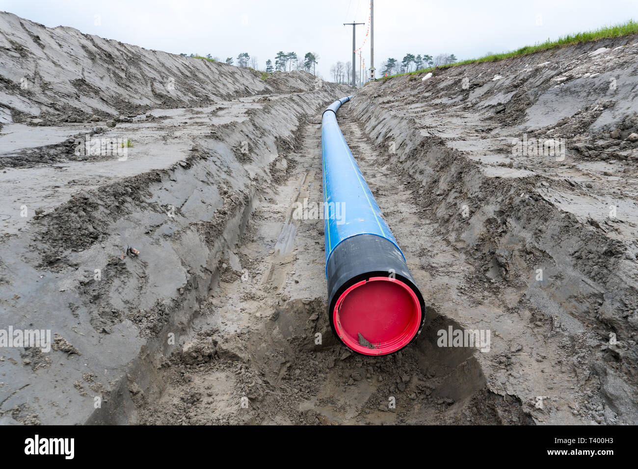 laying large industrial water pipes in an earth and dirt ditch for ...