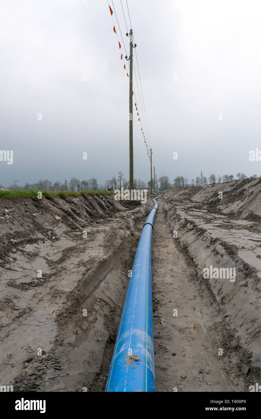 laying large industrial water pipes in an earth and dirt ditch for ...