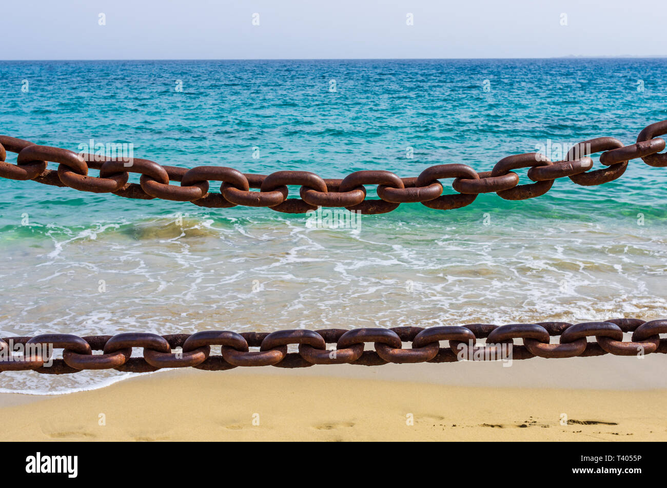 Thick rusty chains with the beach, the sand and the sea in background ...