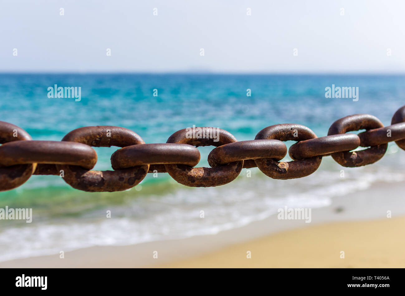 Thick rusty chains with the beach, the sand and the sea in background ...