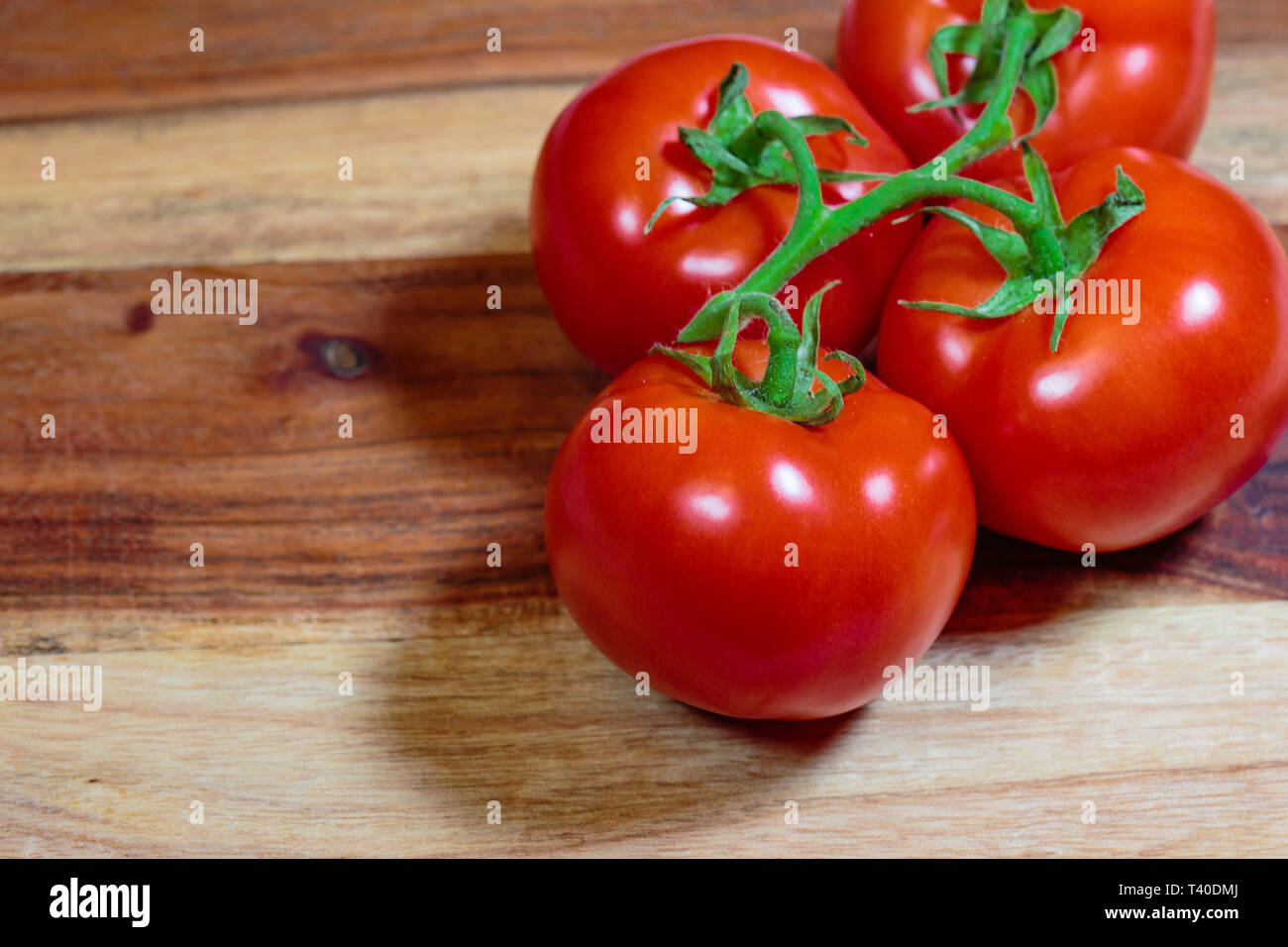Four tomatoes on a green vine laying on a cuttung board Stock Photo - Alamy