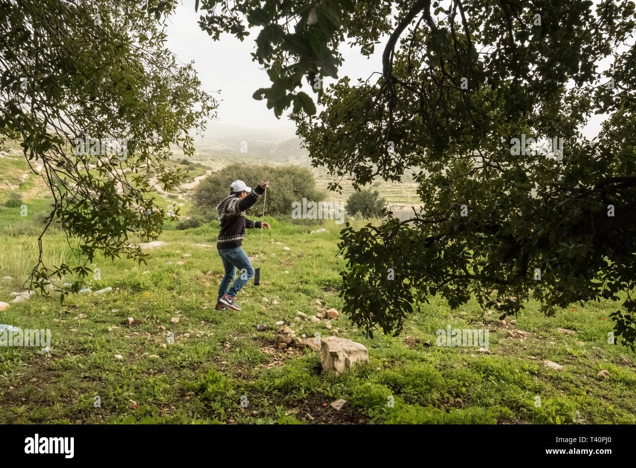 A Palestinian teenager uses a sling shot to throw stones at the Israeli ...