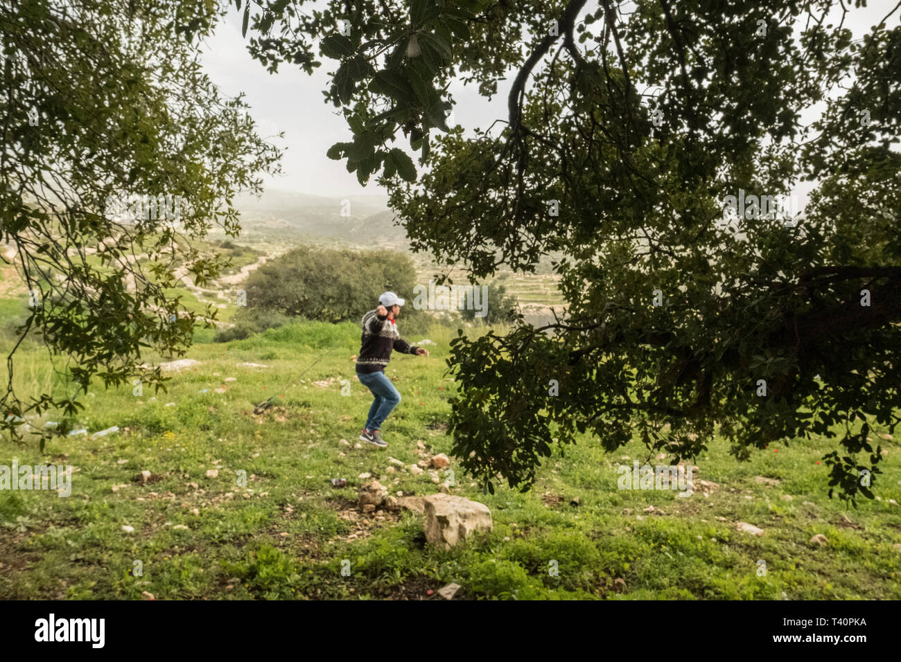 A Palestinian teenager uses a sling shot to throw stones at the Israeli ...