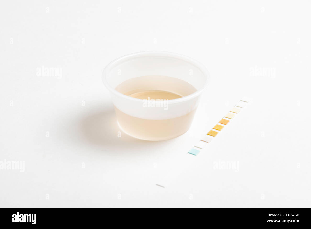 A urine sample in a plastic container with a reagent strip set on a ...