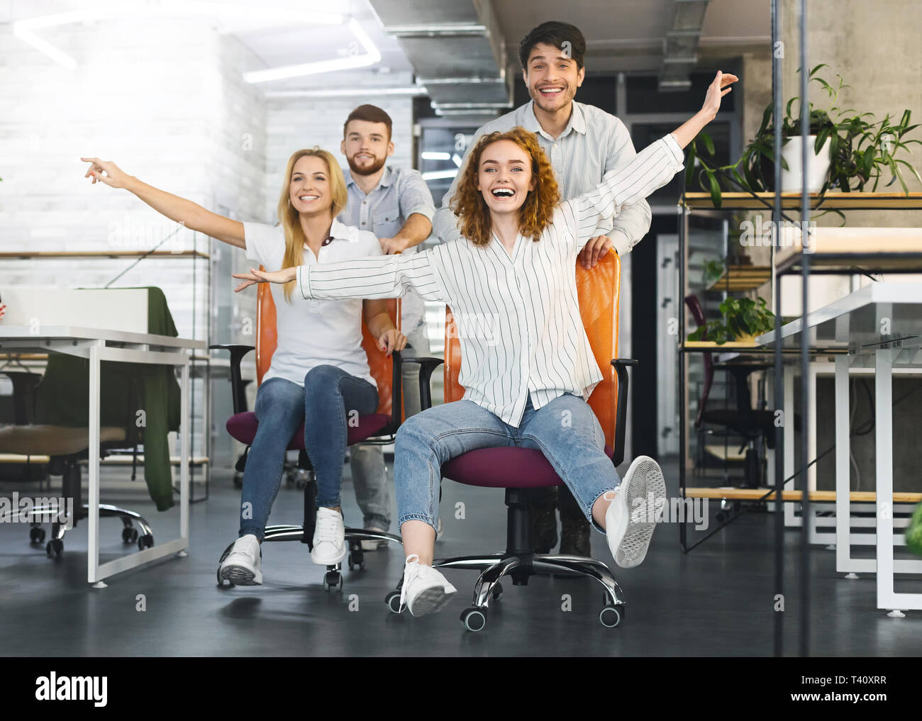 Happy colleagues having fun at workplace, making office chair race ...