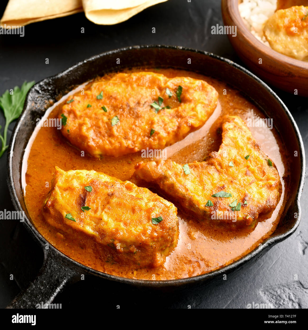 Close up of fish curry in pan on black stone table. Indian style food ...