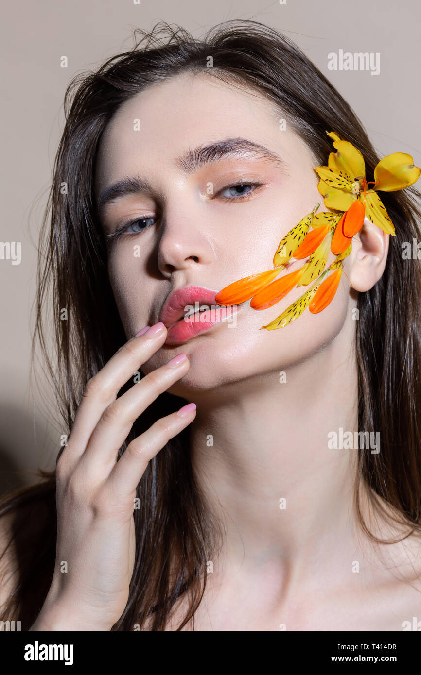 Appealing model with flower in hair touching her lips while posing ...